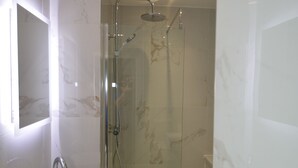 Casa de banho moderna com chuveiro envidraçado, lavatório branco e espelho sobre o lavatório.