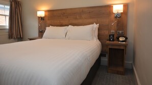 Uma cama bem arrumada com lençóis brancos, duas luminárias de cabeceira e uma cabeceira de madeira.