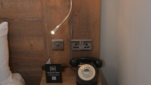 Uma mesa de cabeceira de madeira com uma lâmpada, um telefone rotativo e uma placa para The Rugby Hotel.