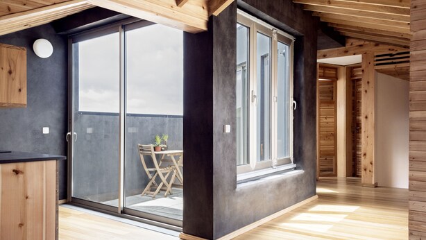 Interior moderno com uma grande porta de vidro deslizante que dá para uma varanda, vigas de madeira no teto e uma parede escura.
