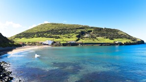 Paisagem costeira com uma colina, águas azul-claras e alguns edifícios na encosta.