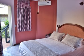 Quarto com cama, cortinas xadrez, ar condicionado e vista para o exterior.
