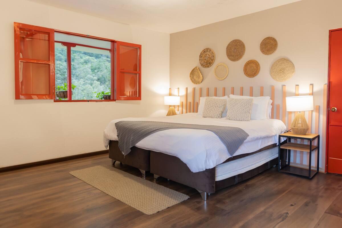 Quarto com cama, chão de madeira, janela com portadas, decoração na parede e abajures.
