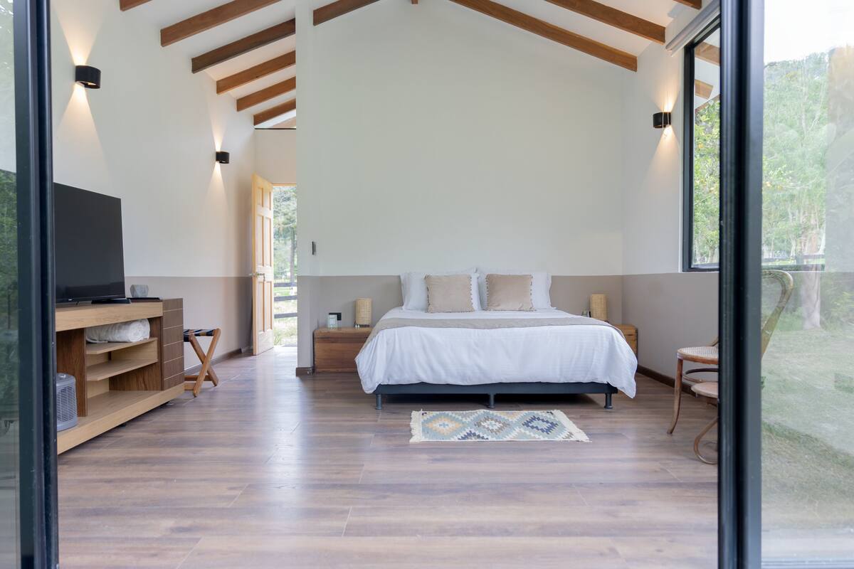 Quarto moderno com uma cama grande, soalho de madeira e uma televisão numa prateleira embutida.