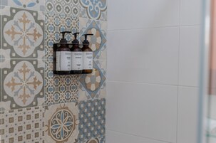 Casa de banho com azulejos estampados e uma prateleira com dois frascos de shampoo e condicionador.