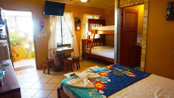 Quarto de hotel com beliche, escrivaninha com cadeira, televisão e janela com cortinas.