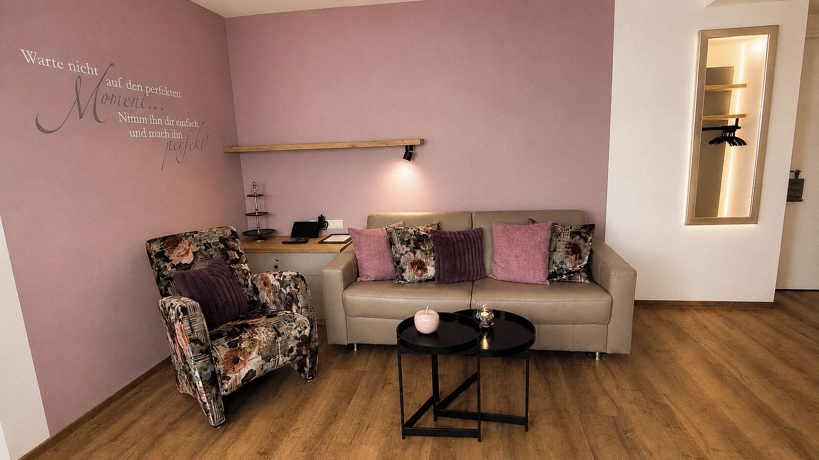 Quarto com sofá, cadeira, mesa pequena e luminária na parede.