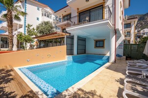 Piscina com borda revestida, rodeada por um deck de madeira e espreguiçadeiras.