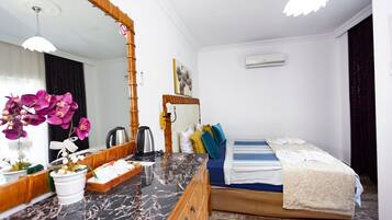 Quarto de hotel com cama, cómoda de madeira, bancada de mármore, pia, espelho e luminária no teto.