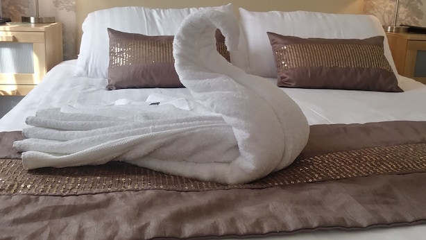 Cama bem arrumada com toalha decorada em forma de cisne, duas almofadas com desenhos em paetês e um edredom marrom com textura.