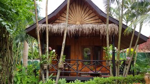 Uma cabana de madeira com telhado de palha, rodeada por vegetação exuberante e plantas tropicais.