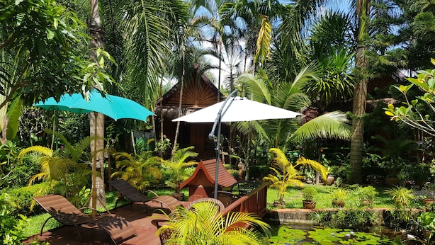 Um jardim tropical com um deck de madeira, cadeiras de descanso e guarda-sóis.