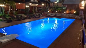 Piscina com espreguiçadeiras e um pequeno deck, cercada por edifícios com arquitetura tradicional.