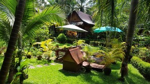 Um jardim tropical com um gazebo de madeira, plantas em vasos e uma cabana com telhado de palha.