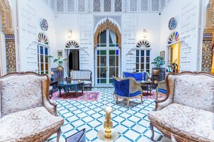 Interior luxuoso com paredes brancas ricamente decoradas, piso xadrez e mobiliário clássico.