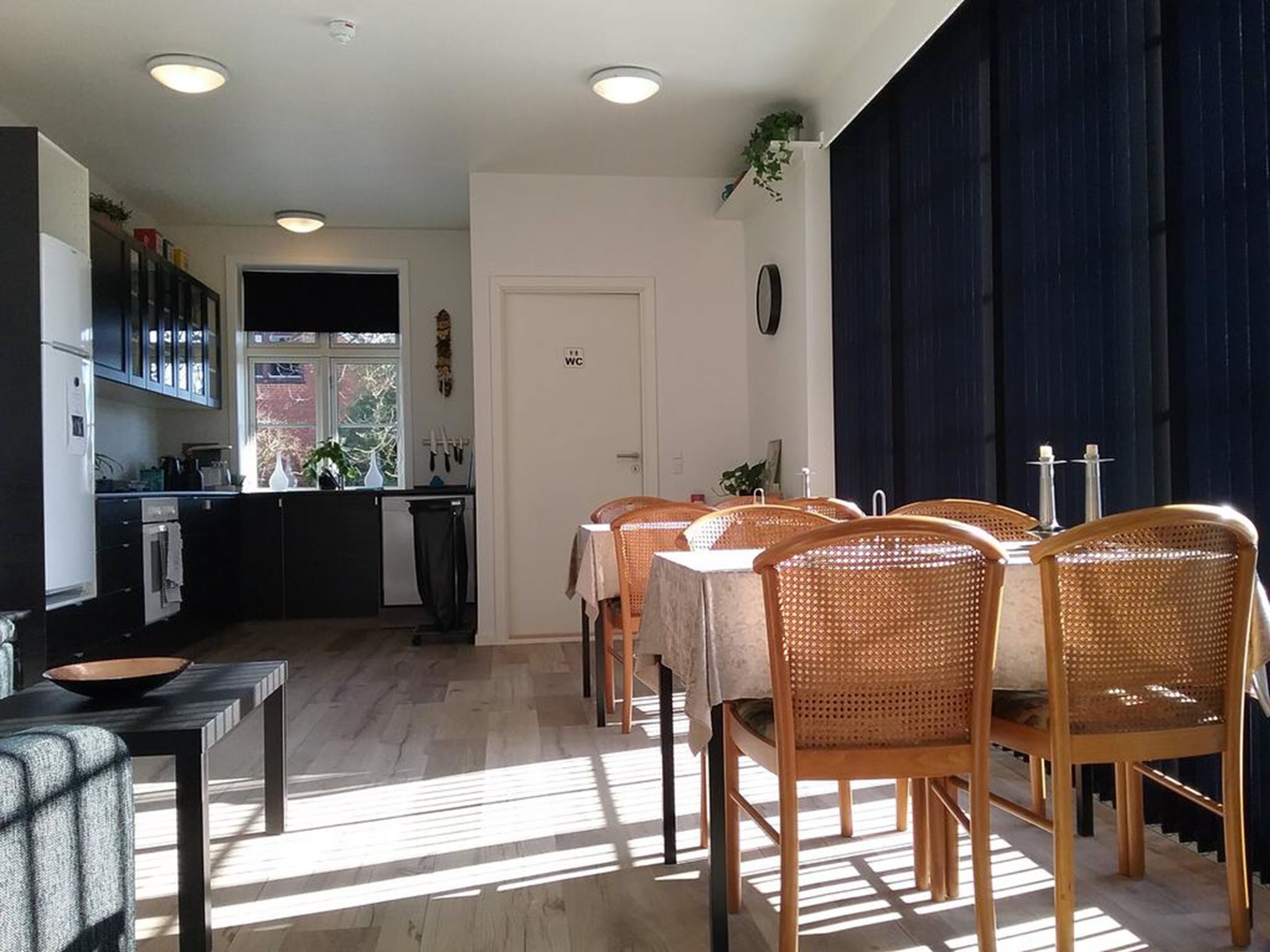 Uma cozinha moderna com armários escuros, uma área de refeições com cadeiras de vime e uma mesa, e vista para o exterior através de uma janela.
