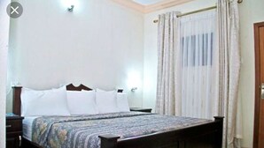 Quarto com cama de madeira, roupa de cama branca e cortina.
