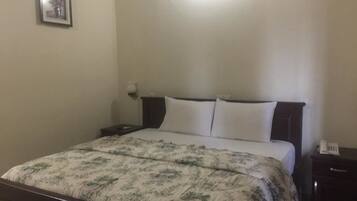 Quarto com uma cama, mesa de cabeceira e telefone fixado na parede.