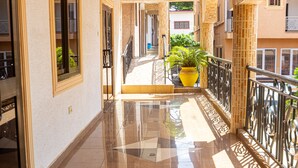Um corredor com piso refletivo, um vaso de planta amarelo e um corrimão de metal.