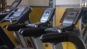 Uma fileira de bicicletas ergométricas em uma academia, com parede amarela e cinza.