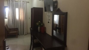 Quarto com escrivaninha de madeira, cadeira, espelho, televisão na parede e janela com cortinas.