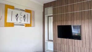 Quarto moderno com ventilador de teto, televisão de tela plana montada e uma obra de arte botânica emoldurada na parede.