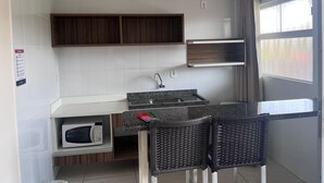 Cozinha compacta com azulejos brancos, armários de madeira escura, micro-ondas e janela com cortinas.