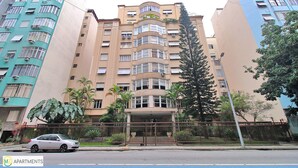 Um edifício residencial com vários andares, varandas, portão fechado e um carro estacionado na frente.