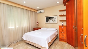 Quarto com cama, mesa de cabeceira, guarda-roupa e ar condicionado fixado na parede.