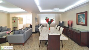 Uma sala de estar moderna com área de jantar, sofá, mesa de centro e televisão.
