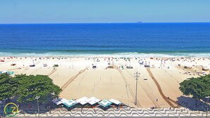 Uma praia com areal, guarda-sóis e pessoas.