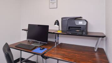 Uma mesa com um laptop, um computador desktop, uma impressora, uma luminária de mesa e uma cadeira.
