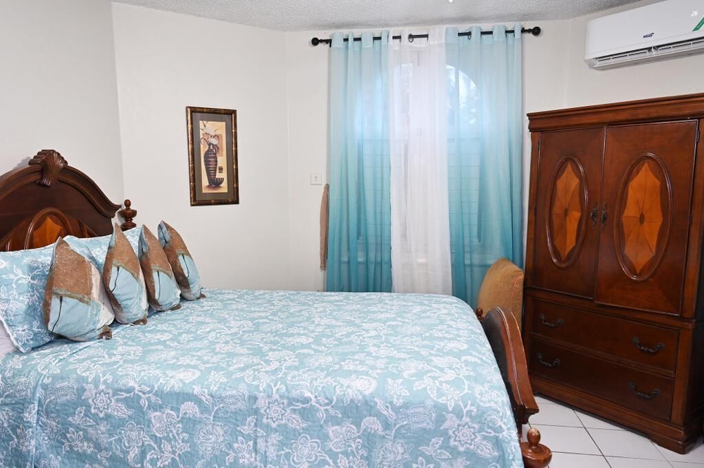 Quarto com cama, guarda-roupa de madeira, quadro emoldurado na parede e janela com cortinas.