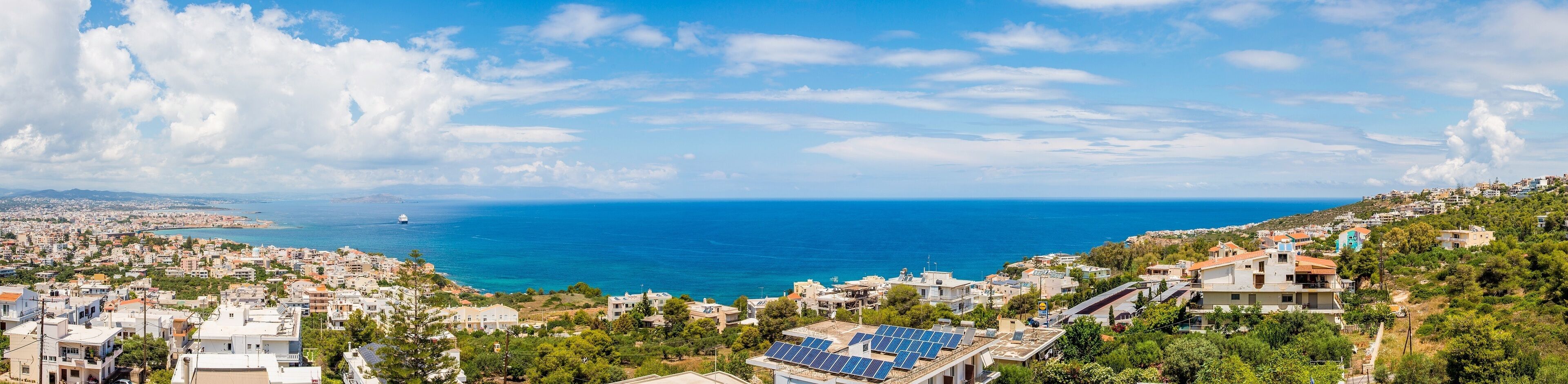 Uma vila costeira com vista para o mar, edifícios com painéis solares e um céu claro.