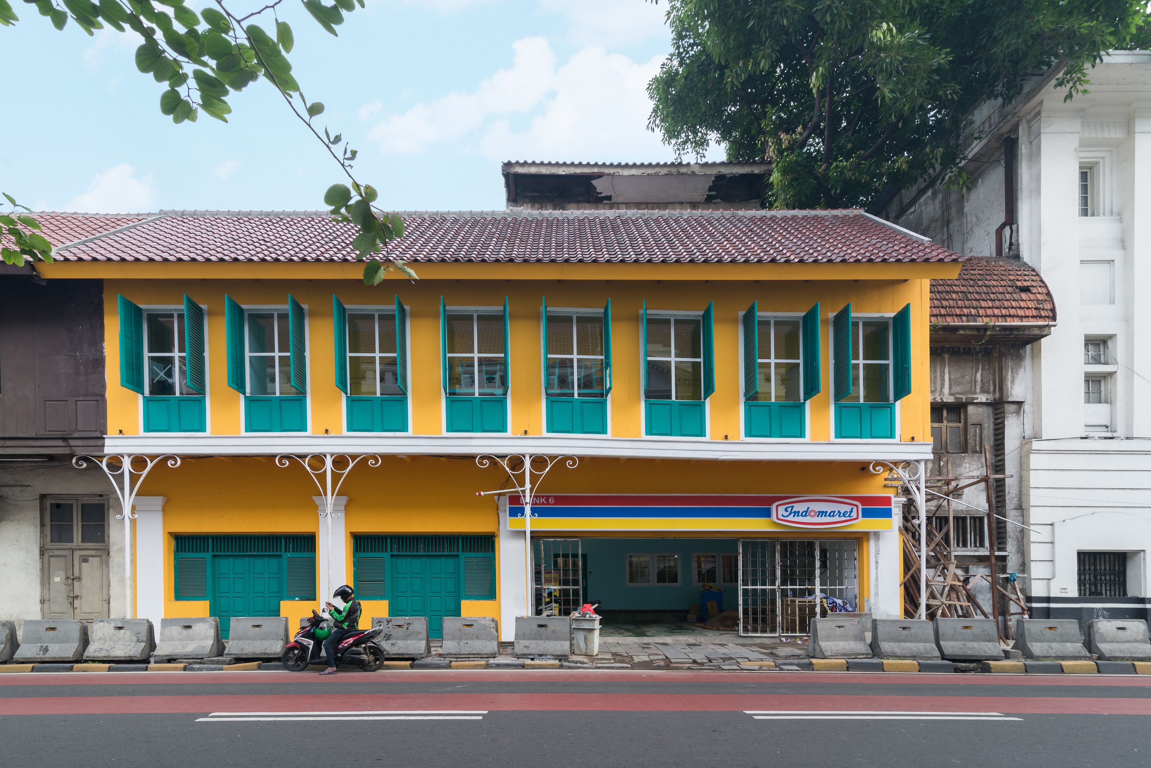 Um edifício amarelo com persianas verdes e uma placa da Indomaret.