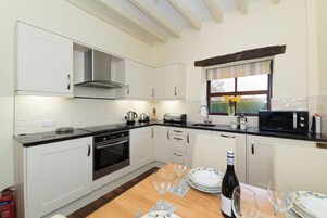 Cozinha moderna com armários brancos, forno embutido, micro-ondas e área de jantar com mesa posta para dois.