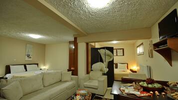 Quarto de hotel com sofá, poltrona, mesa de jantar e televisão.