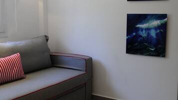 Uma sala de estar moderna com um sofá cinzento, uma mesinha de madeira com uma vela e flores, e duas pinturas abstratas na parede.