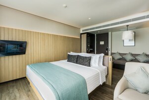 Quarto de hotel com uma cama, um sofá, uma televisão e uma porta que dá para um banheiro.