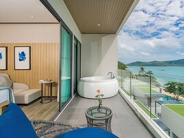 Uma varanda com banheira de hidromassagem, área de estar com sofá e cadeiras, e vista para o mar.