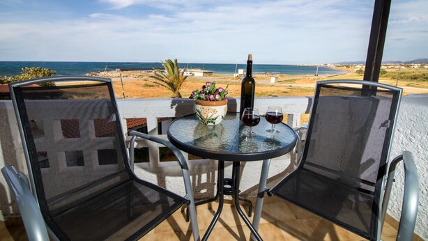 Varanda com duas cadeiras de tela, uma mesa, uma garrafa de vinho e um vaso de flores.