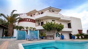 Um edifício de dois andares com piscina, espreguiçadeiras e plantas em vasos.