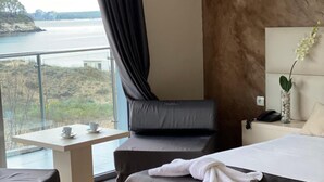 Quarto de hotel moderno com uma cama grande, uma mesinha com duas chávenas, uma cadeira, uma mesa de cabeceira com um telefone e vista para um corpo de água.