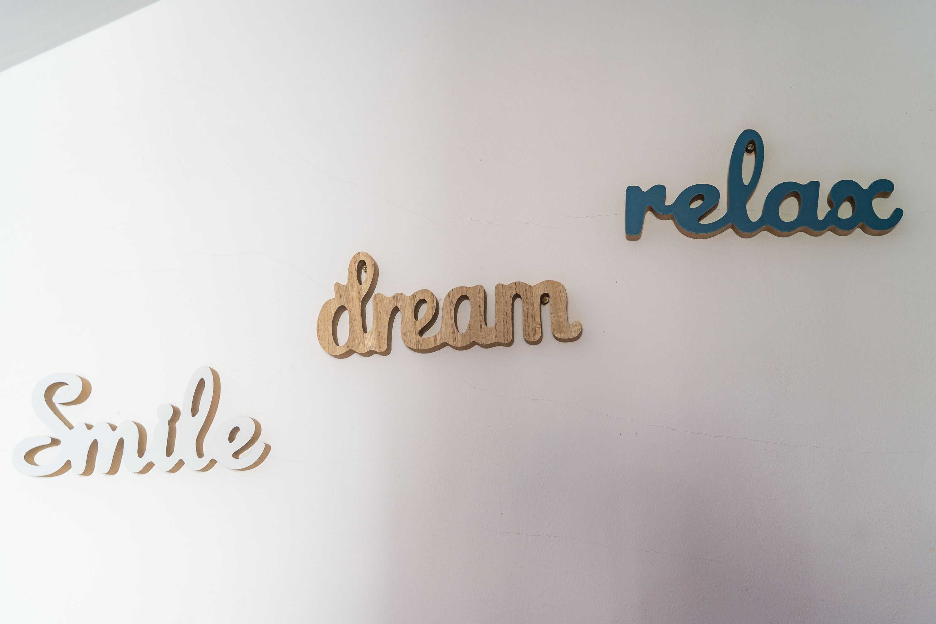 Três letras de madeira recortadas em uma parede: 'dream', 'relax' e 'smile'.