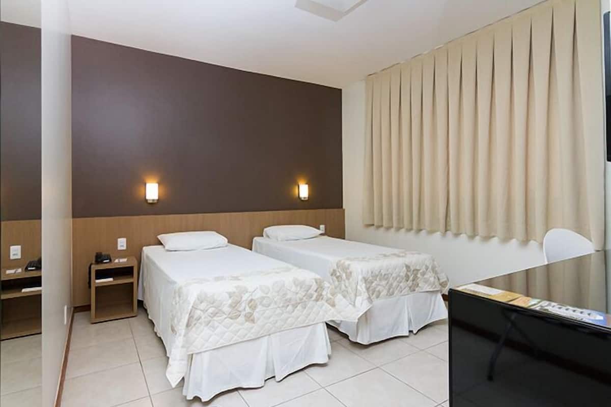 Quarto de hotel com duas camas, uma escrivaninha e uma cadeira.