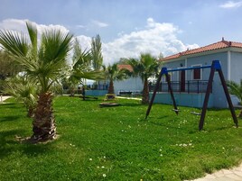 Uma área gramada com palmeiras, balanço e um edifício com telhado de azulejos.