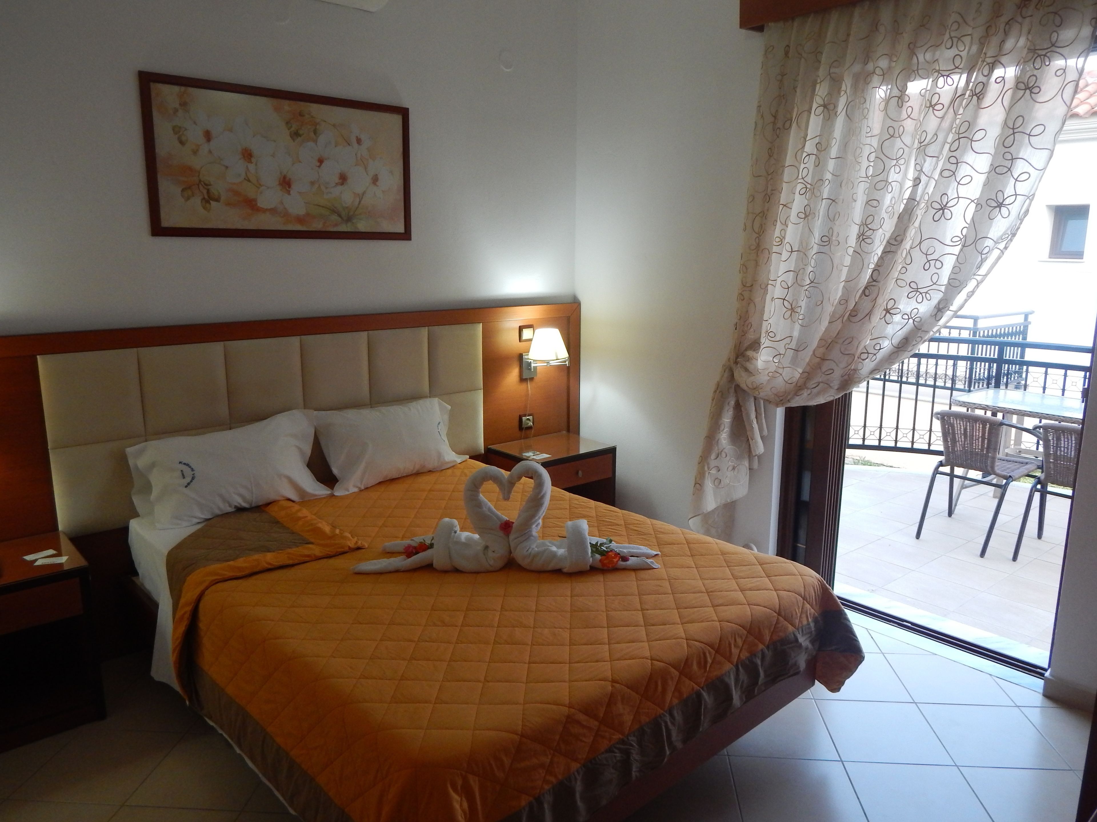 Quarto de hotel com cama, mesa de cabeceira, abajur, quadro na parede e vista para a varanda.