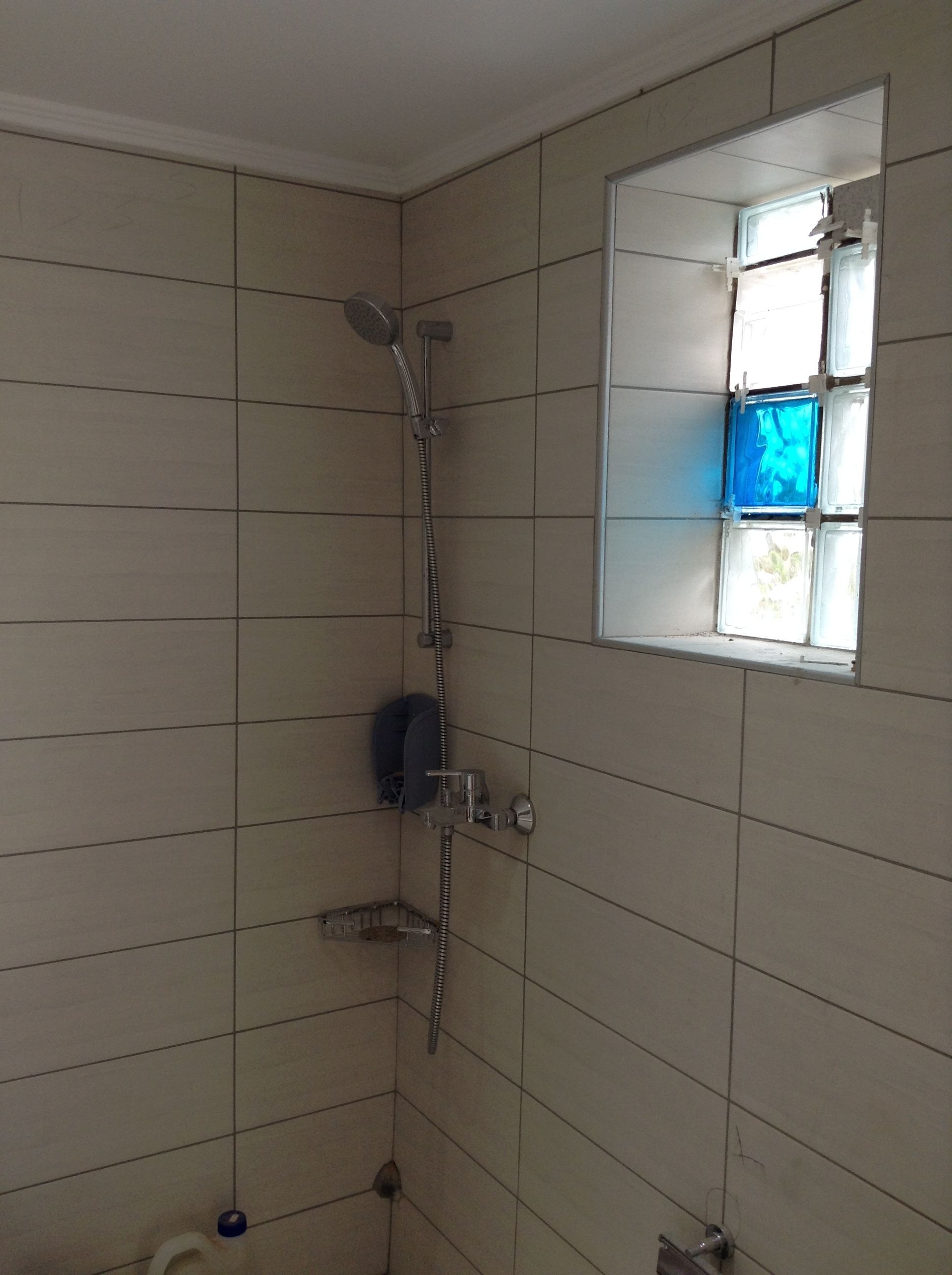 Um espaço de chuveiro pequeno, revestido com azulejos, com um chuveiro manual e uma janela com vidro azulado.