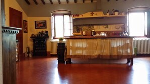 Um quarto amplo com piso de madeira, uma mesa com toalha, um radiador e uma janela com cortinas.