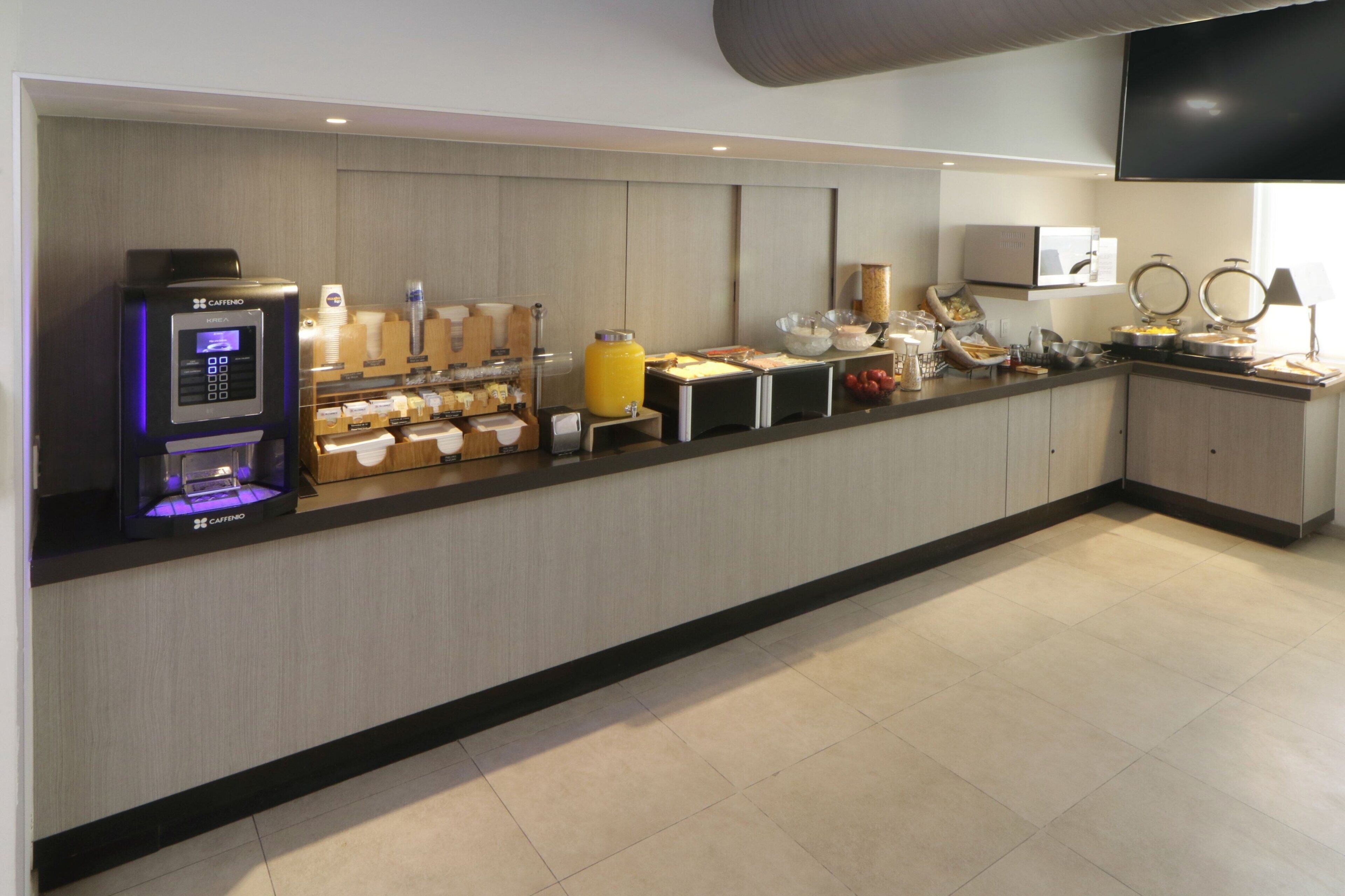 Bancada de café da manhã de hotel, com máquina de café, frutas e cereais.